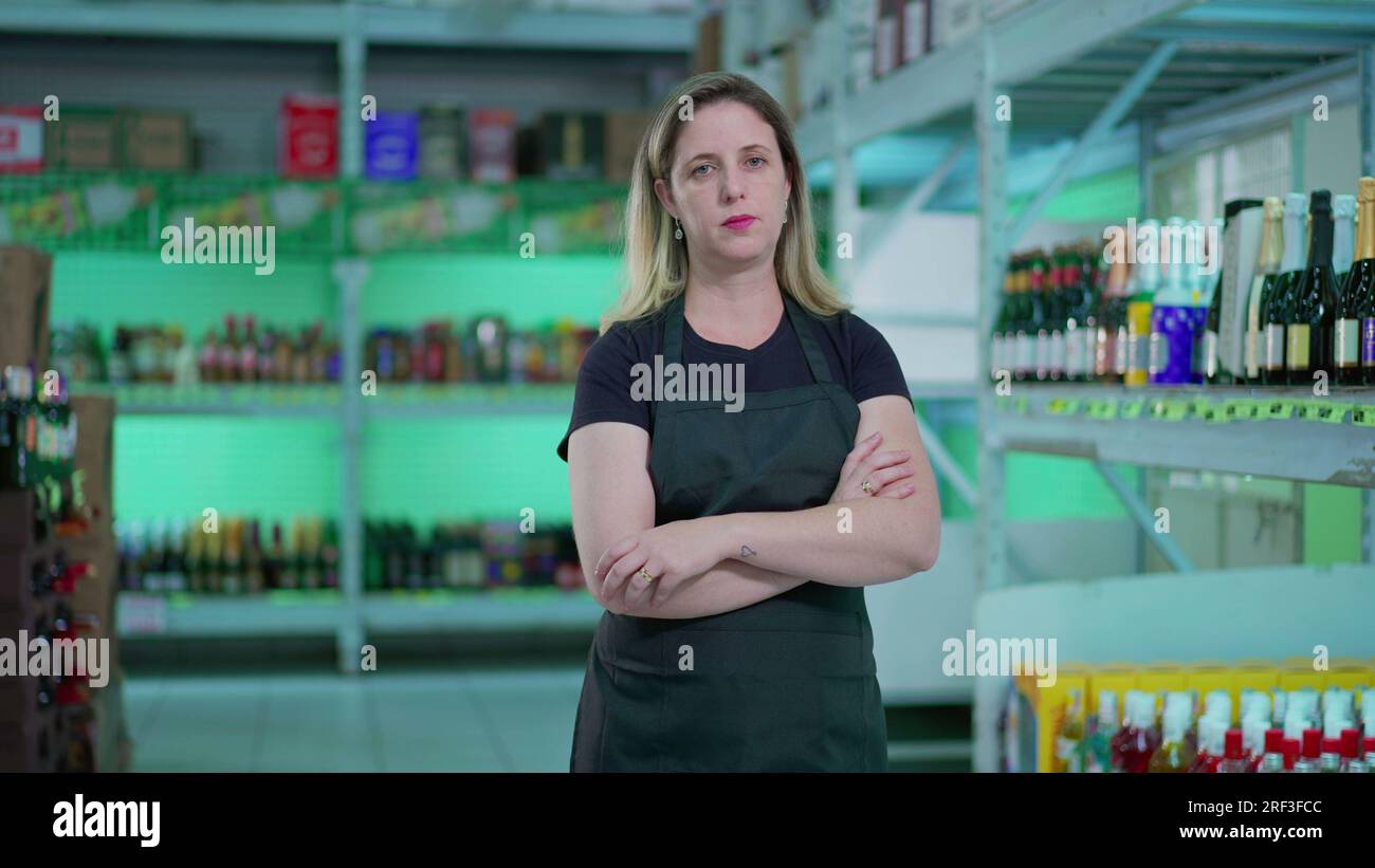 Serious female employee of Supermarket standing at aisle looking at ...