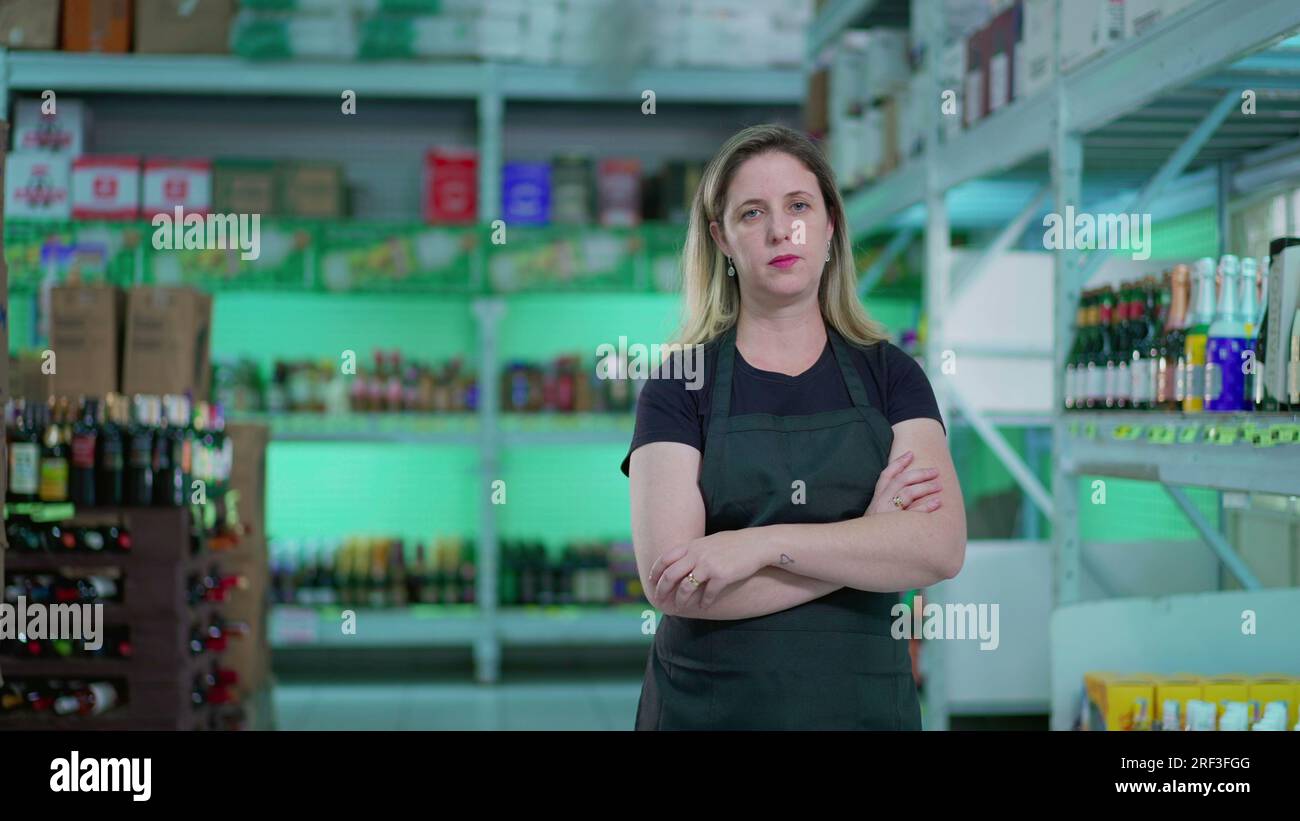 Serious female employee of Supermarket standing at aisle looking at ...