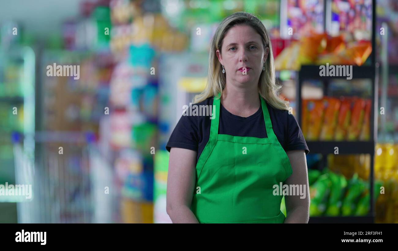 Serious female employee of Supermarket wearing green apron, middle-aged ...