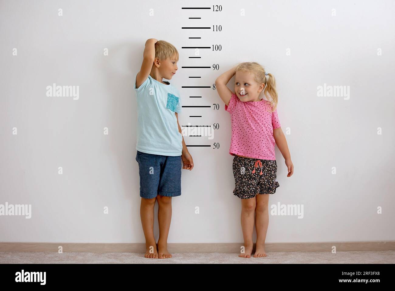 Little children, blond boy and girl, measuring height against wall in ...