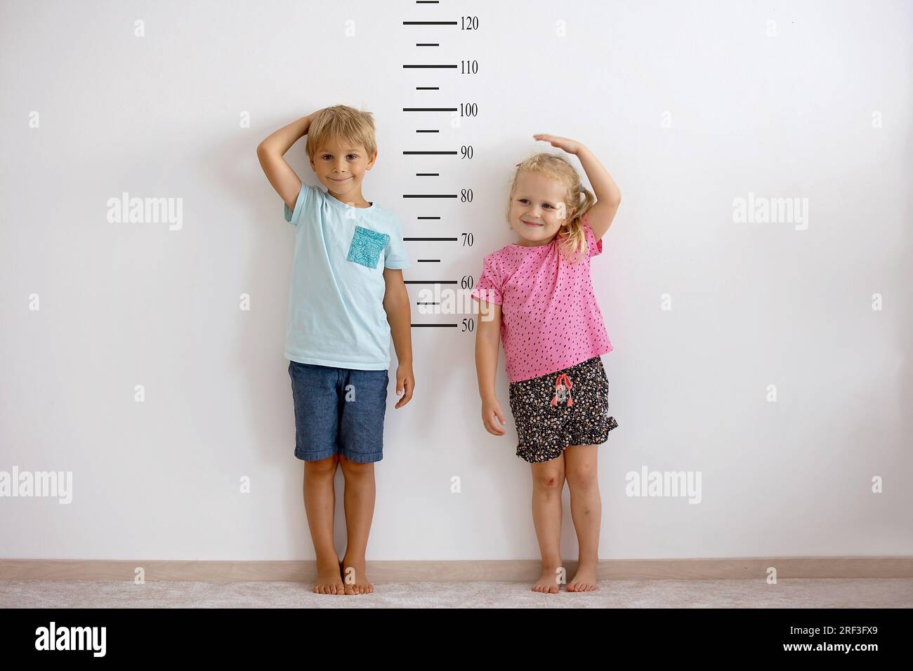 Little children, blond boy and girl, measuring height against wall in ...