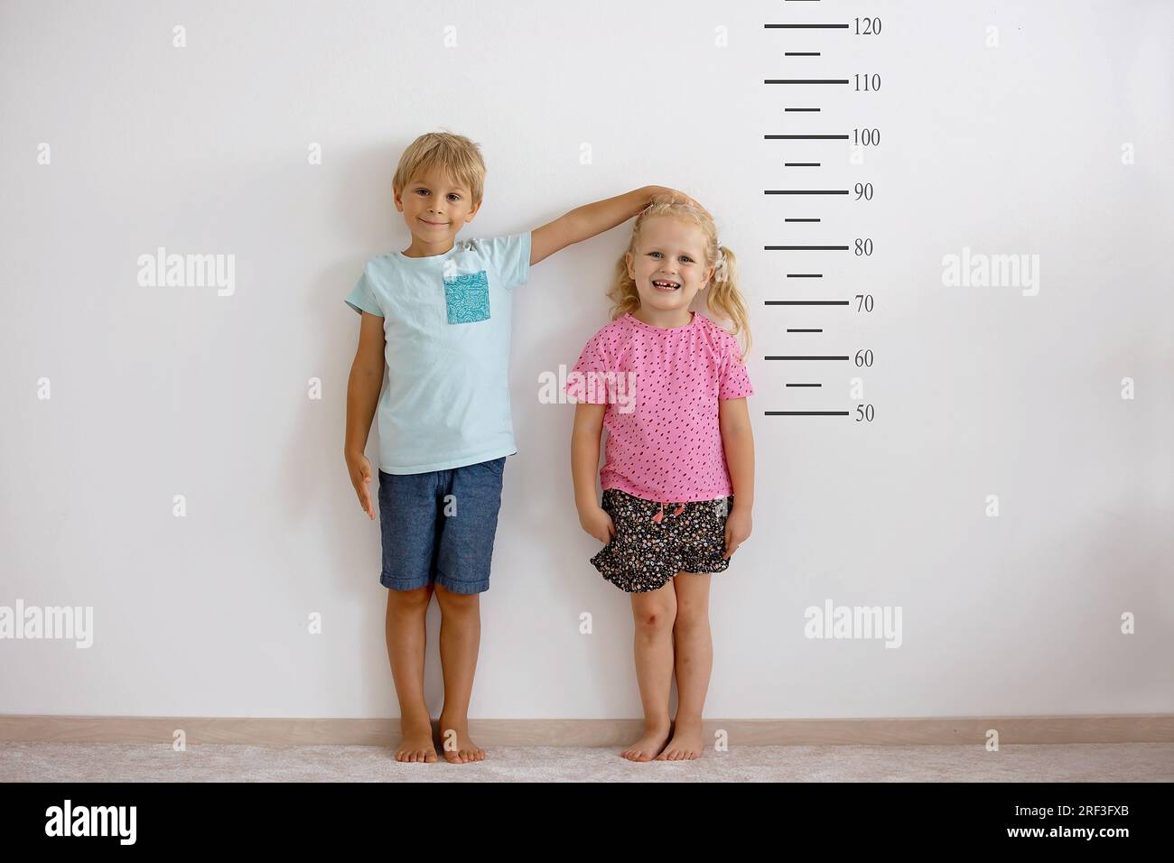 Little children, blond boy and girl, measuring height against wall in ...