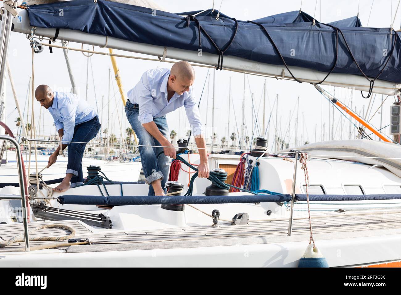 Two men in blue shirts and jeans working on sailing yacht in the port ...