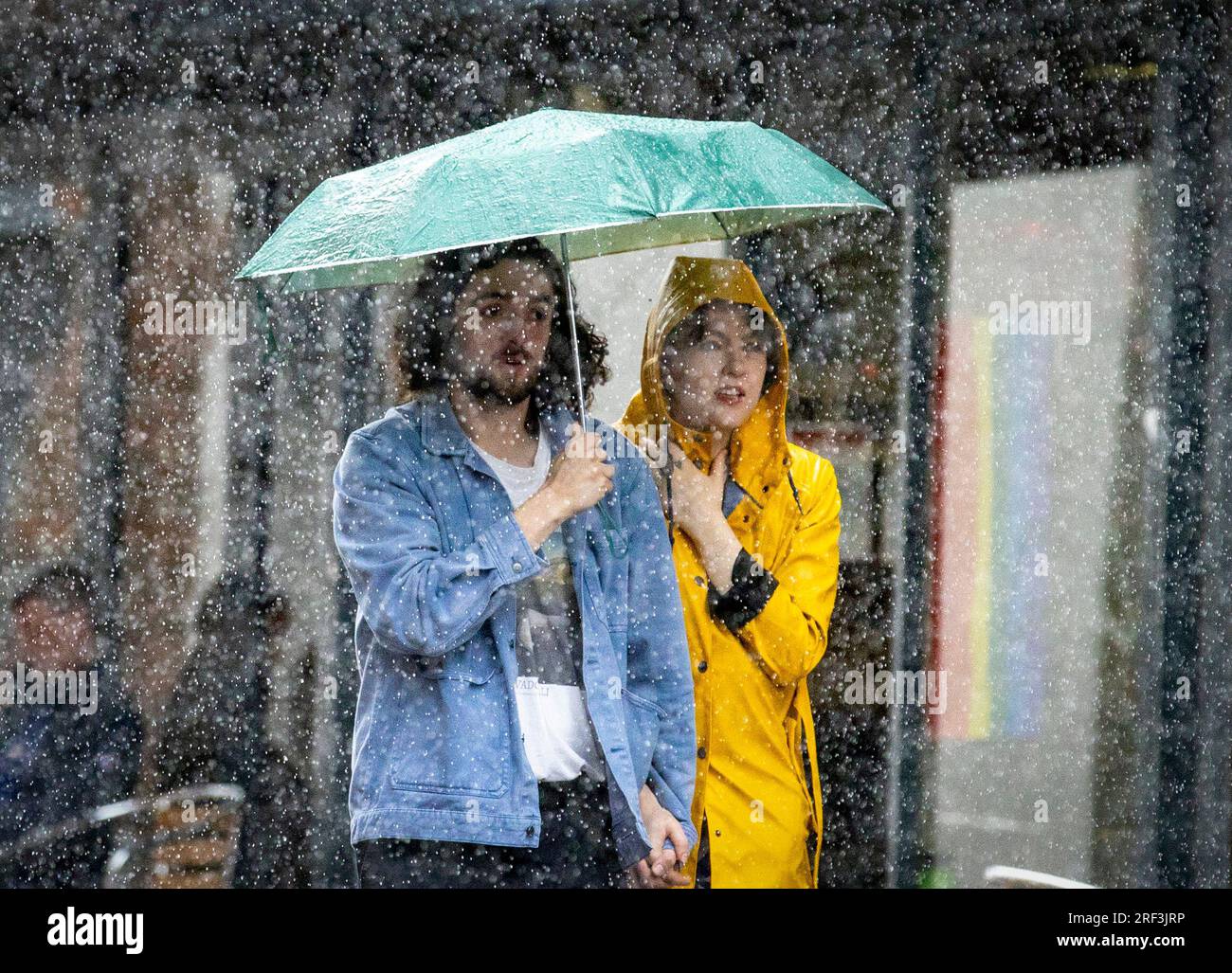 A couple shelter under an umbrella during a heavy downpour of rain in ...