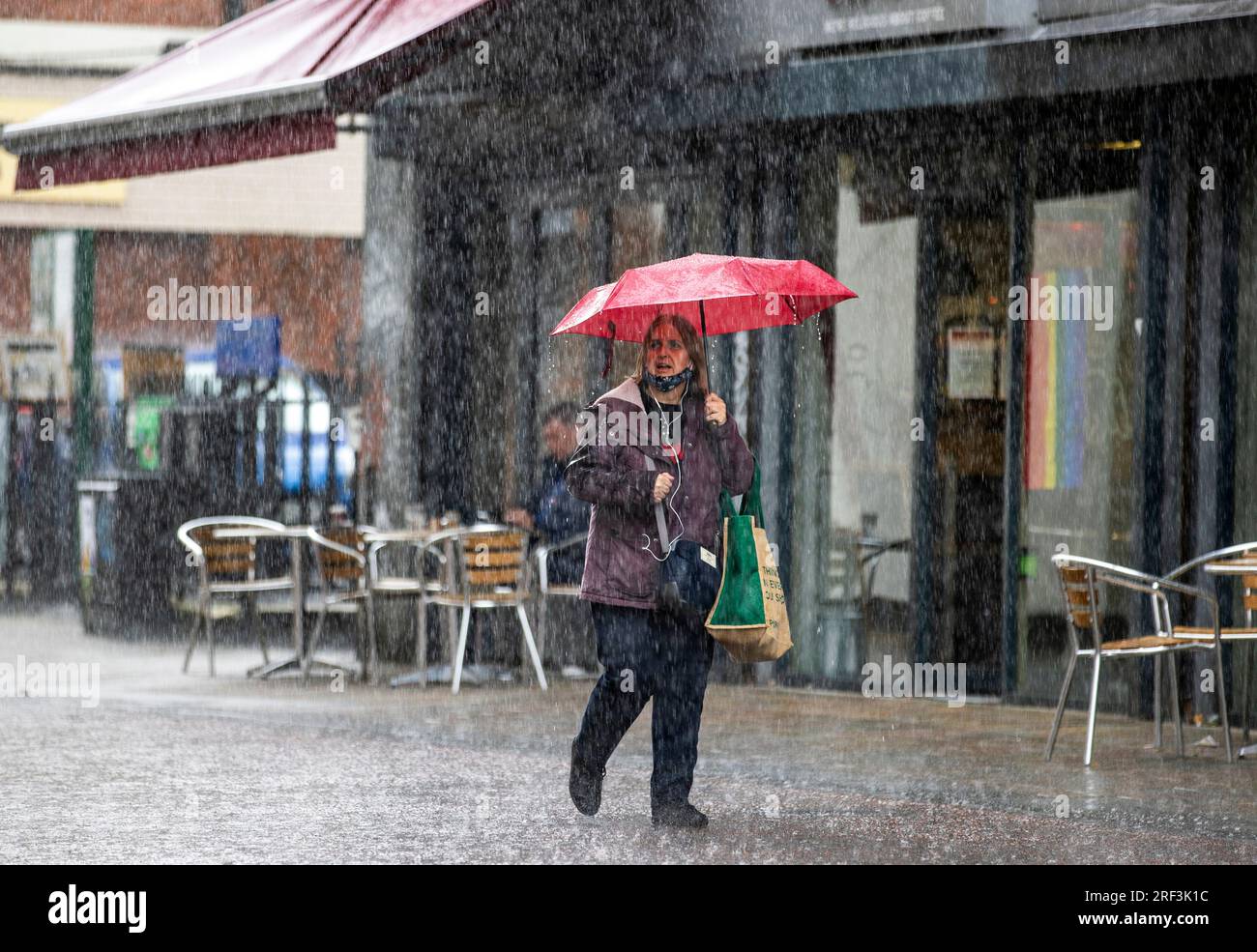 A woman shelters under an umbrella during a heavy downpour of rain in ...