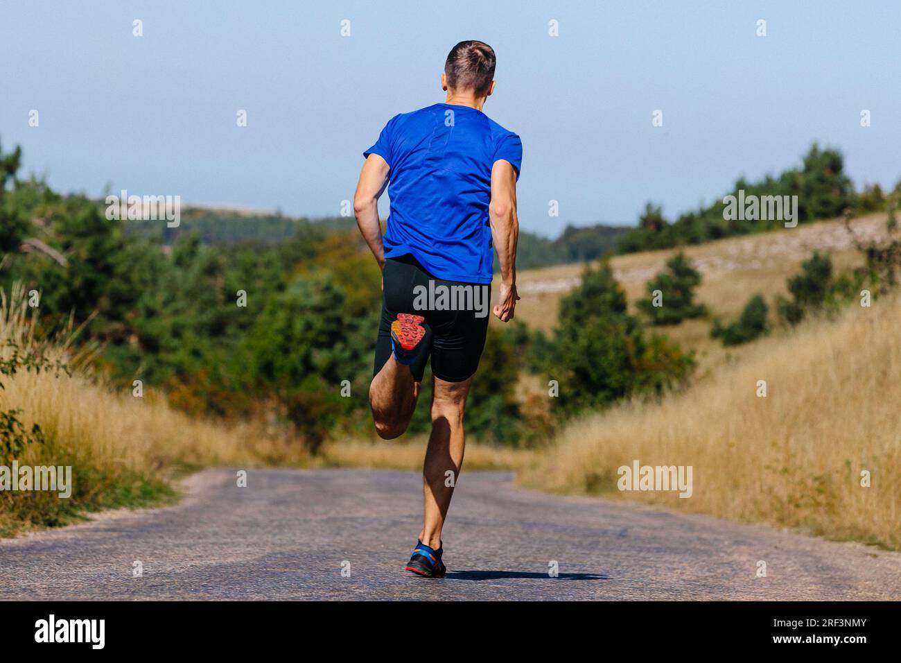 rear view male runner in blue shirt and black tights running road in ...