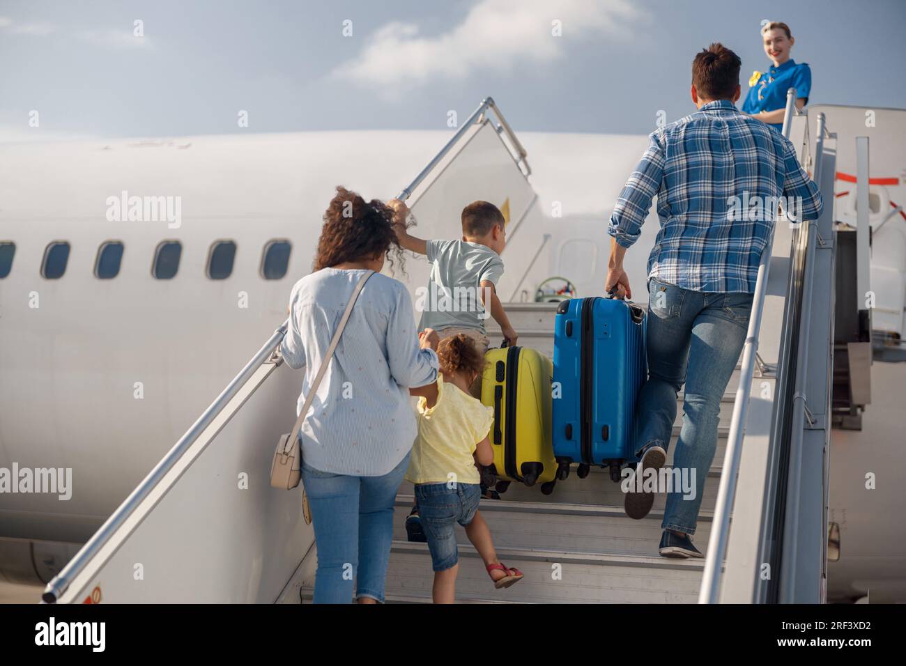 Back view of family of four getting on, boarding the plane on a daytime ...