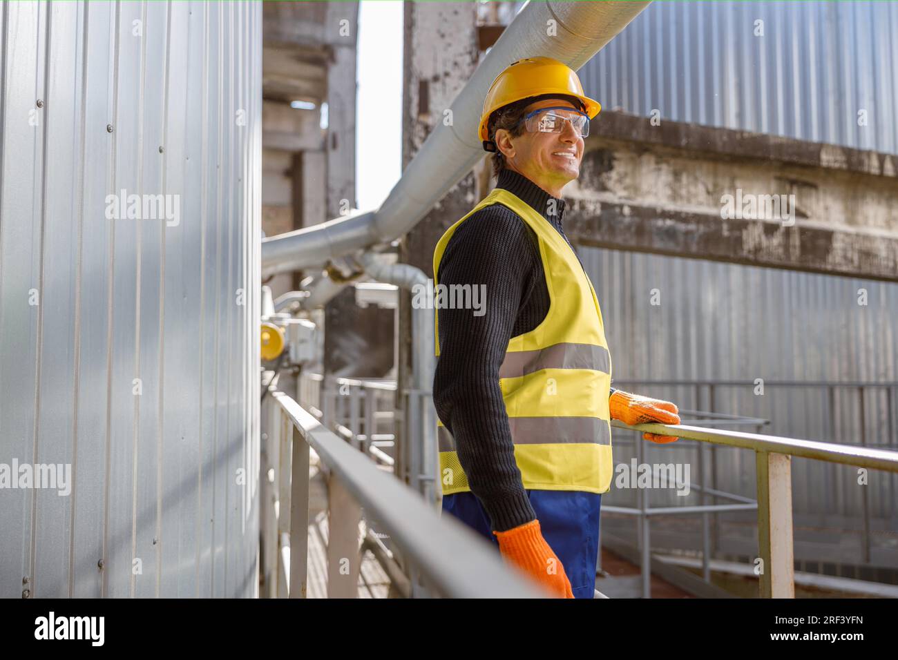 Cheerful male engineer standing near metal pipe at factory Stock Photo ...