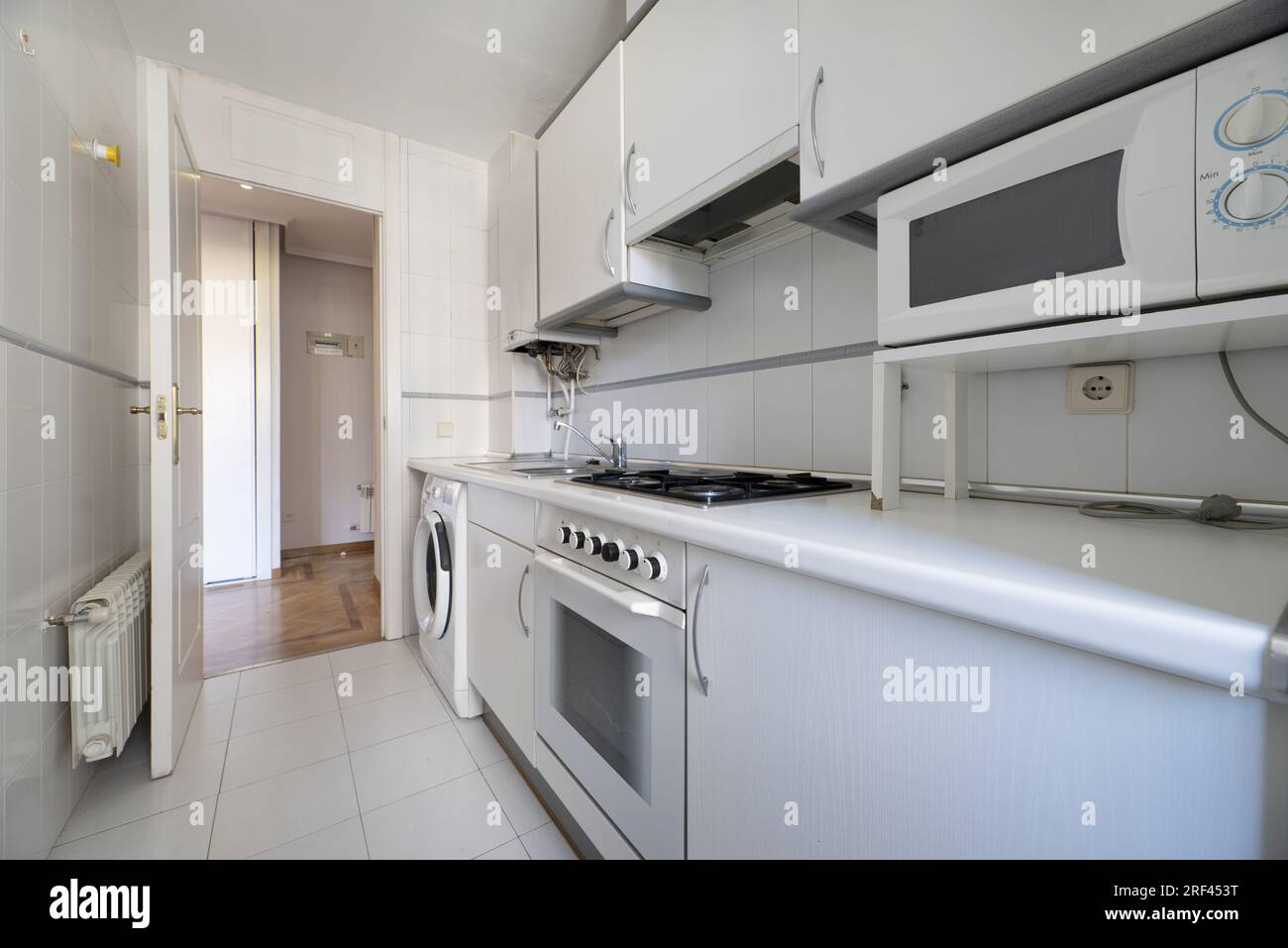 Elongated kitchen with a wall furnished with white furniture, a ...