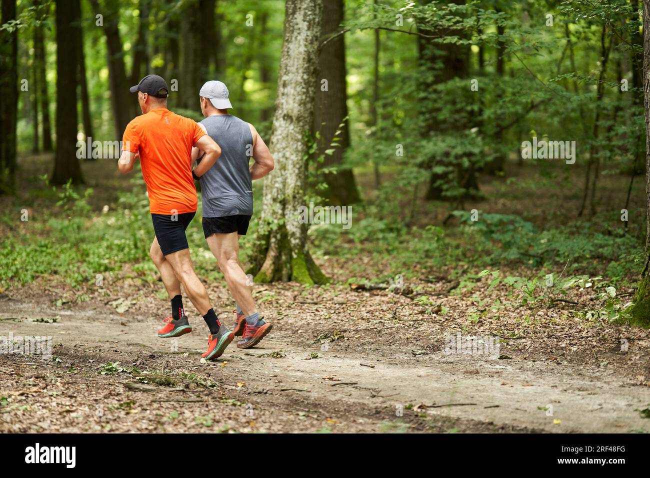 Two male friends running together on a trail through the forest Stock ...