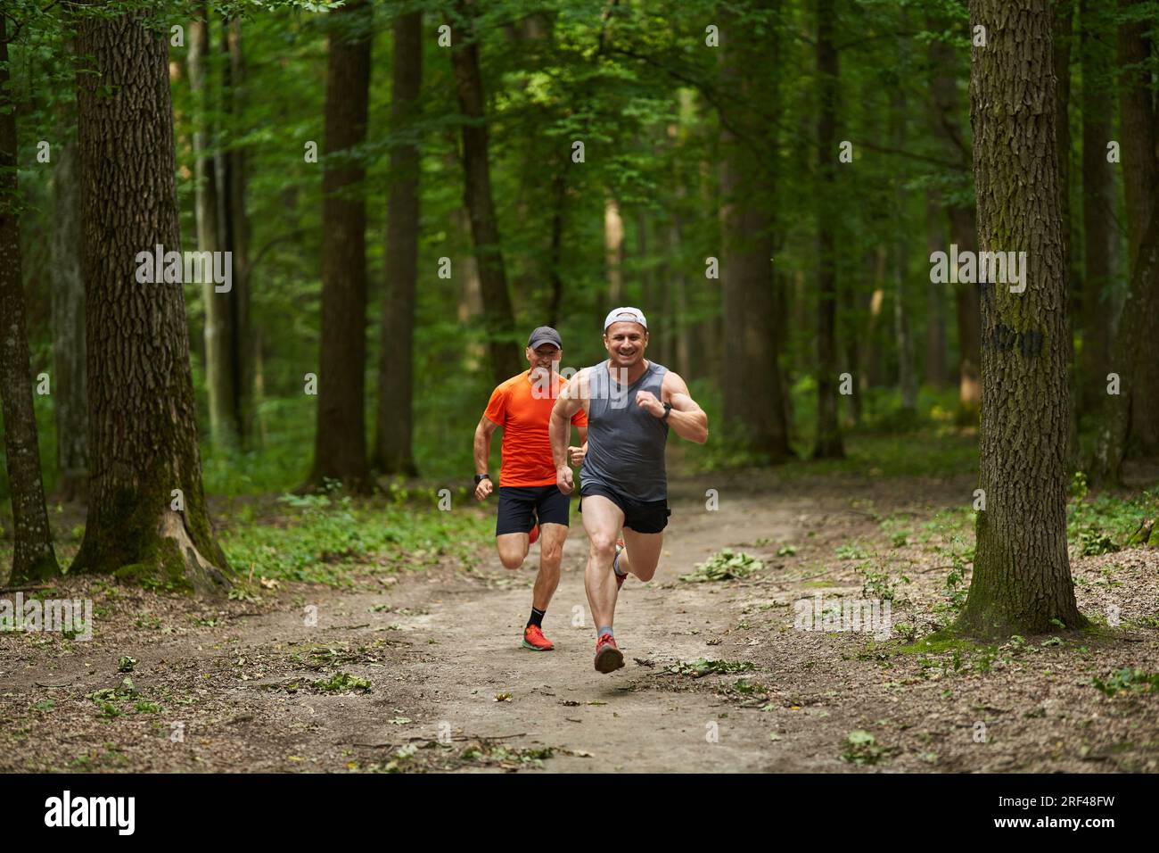 Two male friends running together on a trail through the forest Stock ...