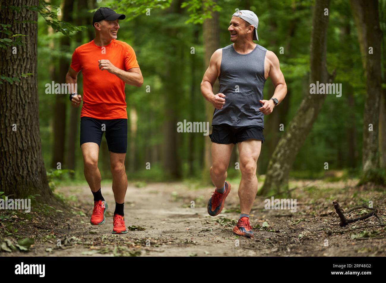 Two male friends running together on a trail through the forest Stock ...