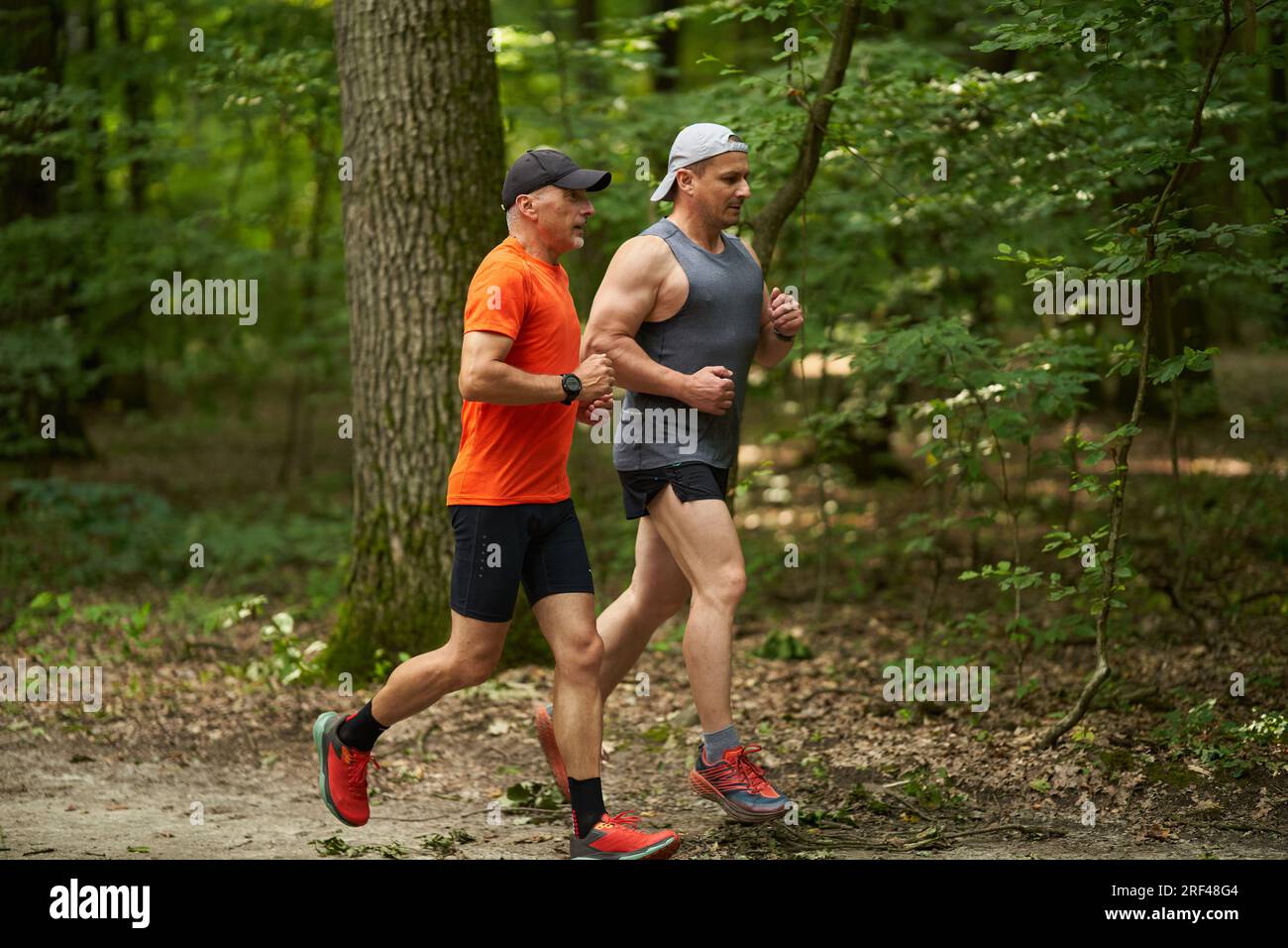 Two male friends running together on a trail through the forest Stock ...