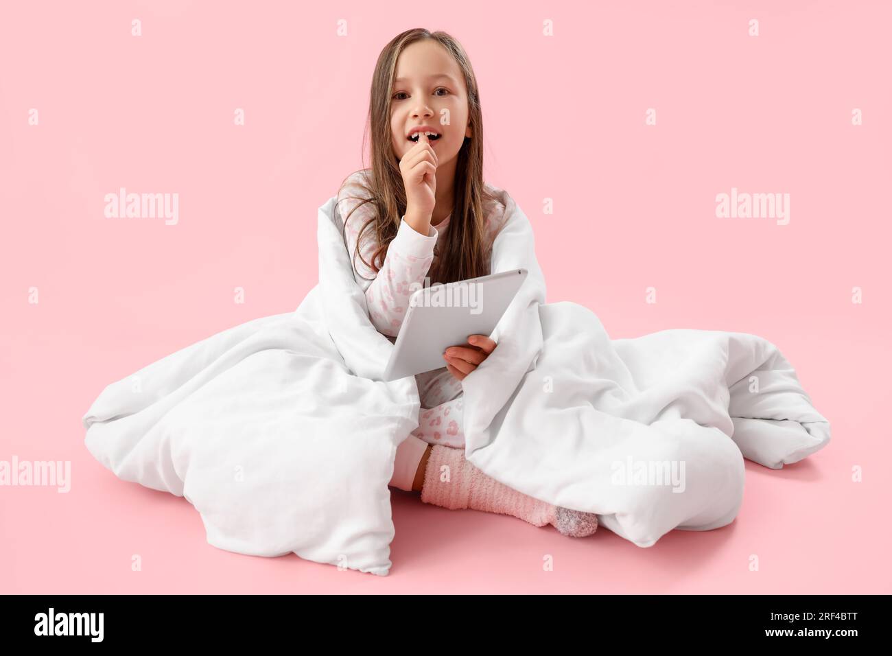 Little girl with blanket and tablet computer biting nails on pink ...