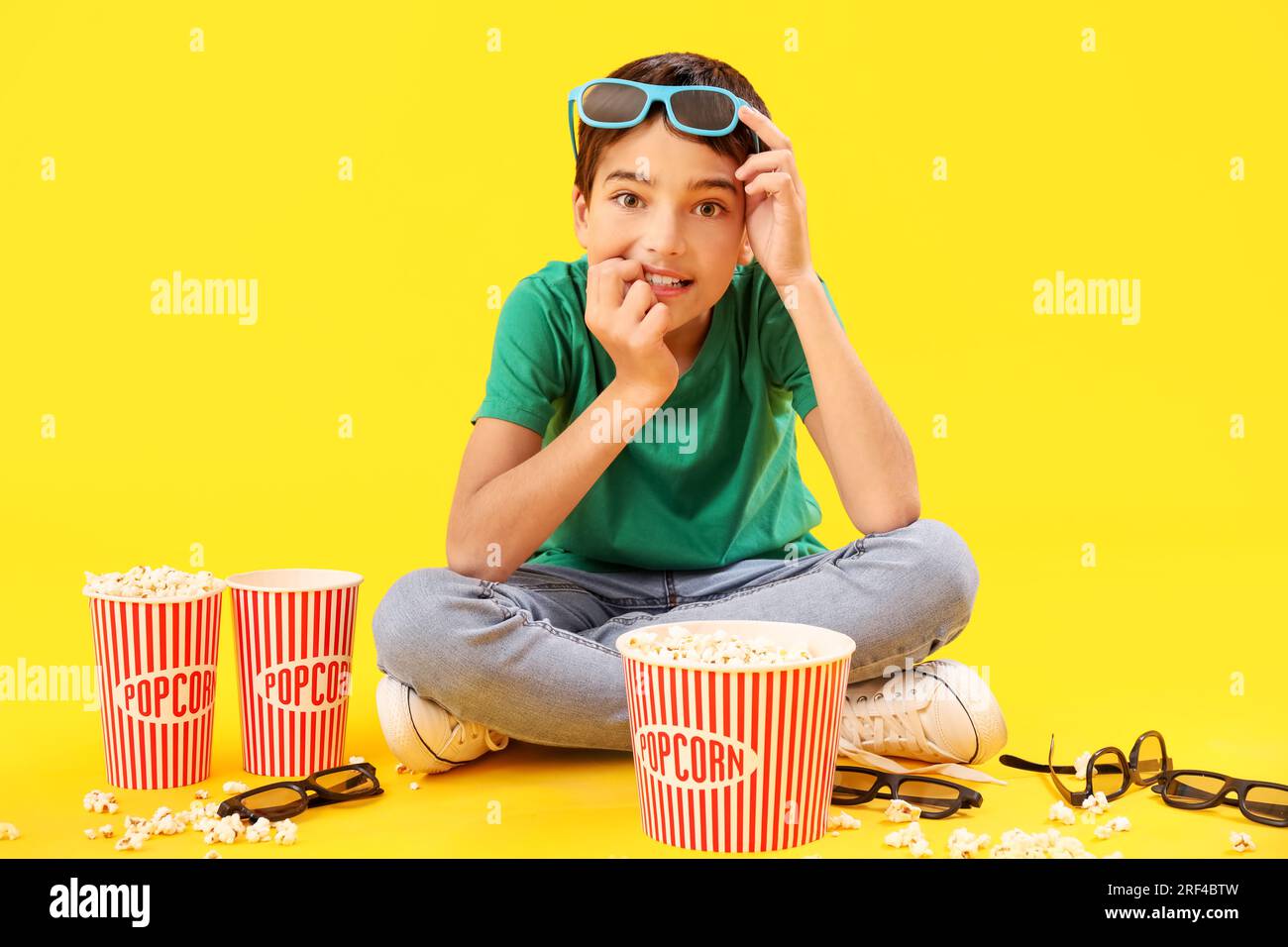 Little boy in 3D glasses with popcorn biting nails on yellow background ...