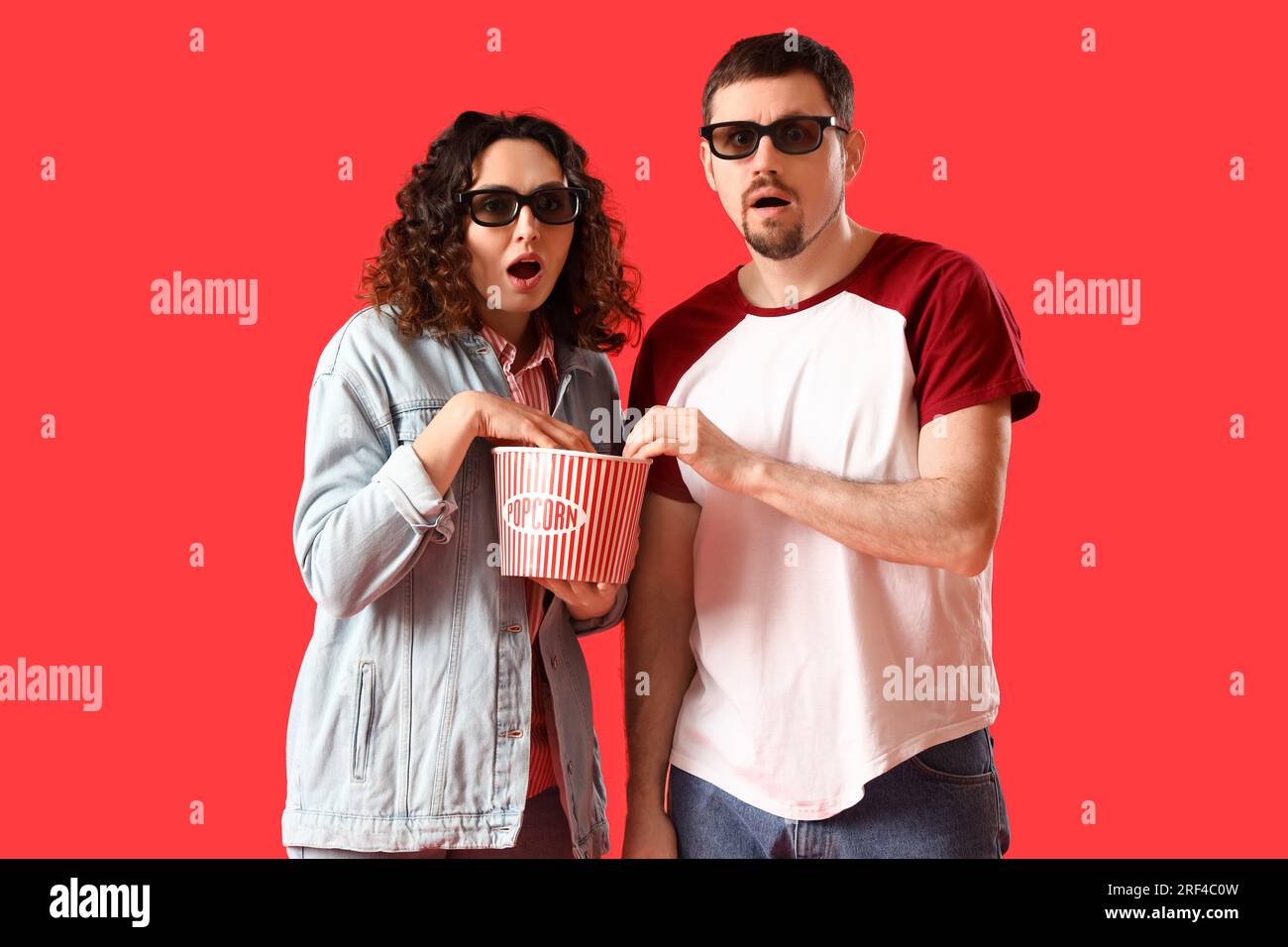 Shocked young couple in 3D glasses with popcorn on red background Stock Photo - Alamy