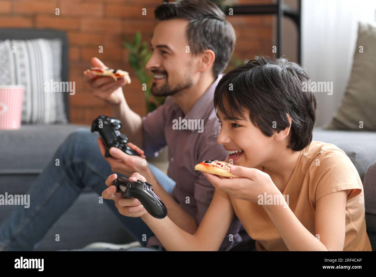 Little boy with his father eating pizza while playing video game at ...