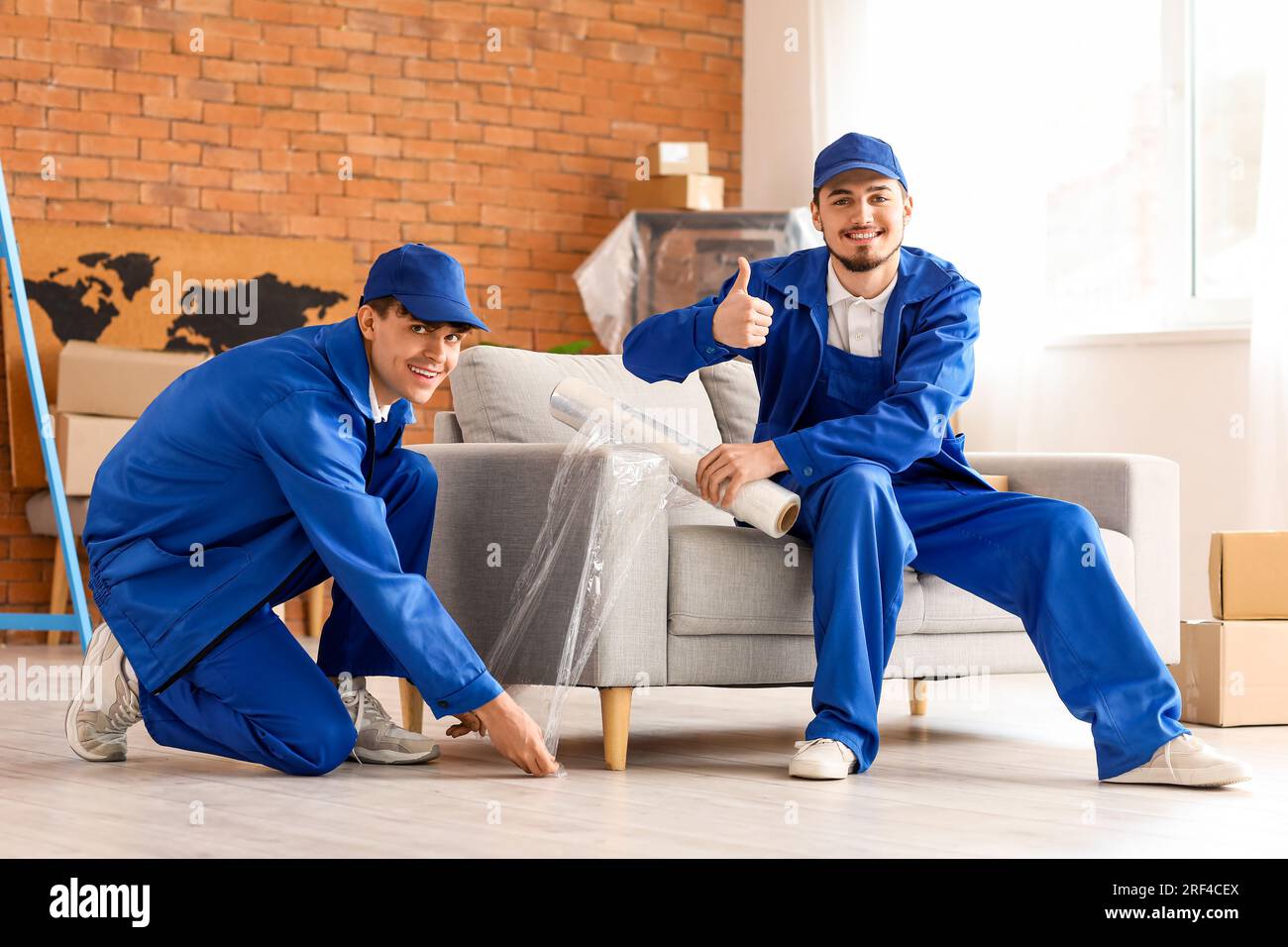 Male movers wrapping sofa with stretch film in room Stock Photo - Alamy