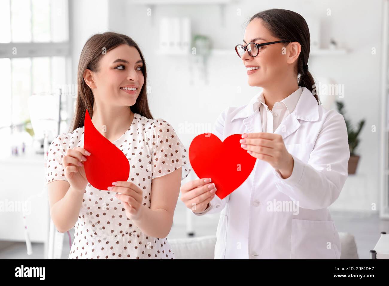 Female doctor with young donor holding paper blood drop and heart in ...