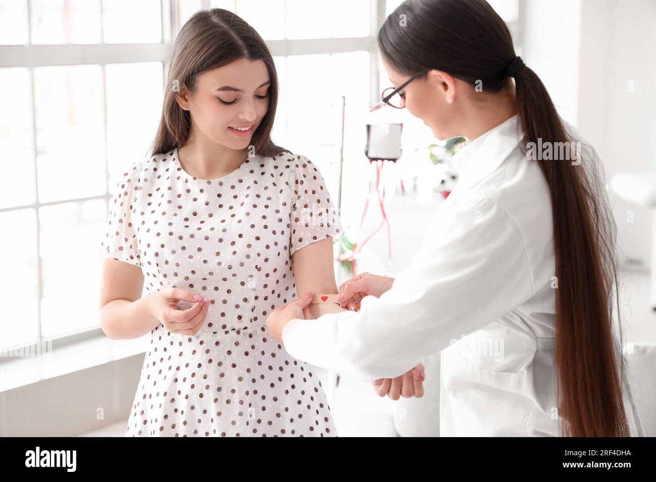 Female doctor applying medical patch on young donor's arm in clinic ...