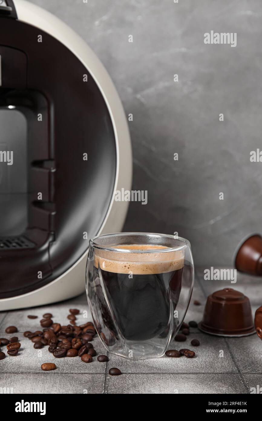 Glass of delicious espresso, capsule coffee maker, pods and beans on ...