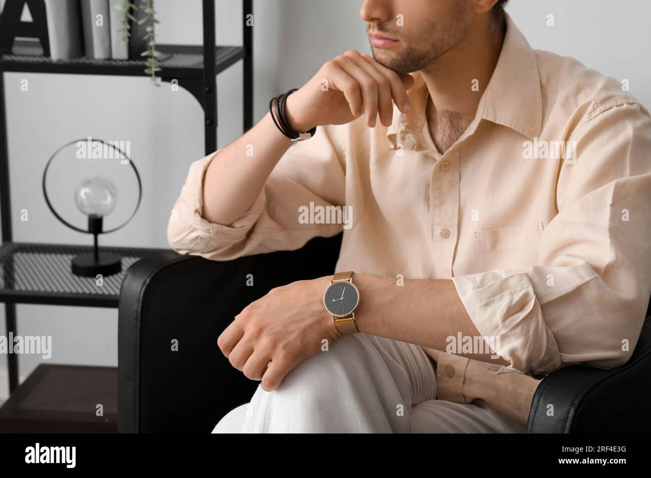 Stylish young man with wristwatch sitting on armchair in room Stock ...