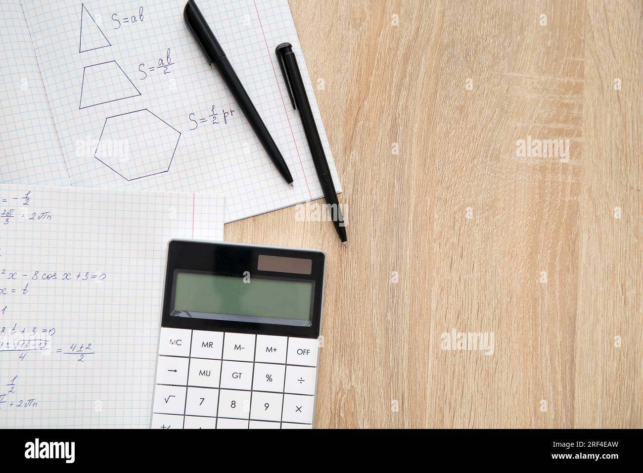 Open copybooks with math formulas, calculator and pens on wooden table ...