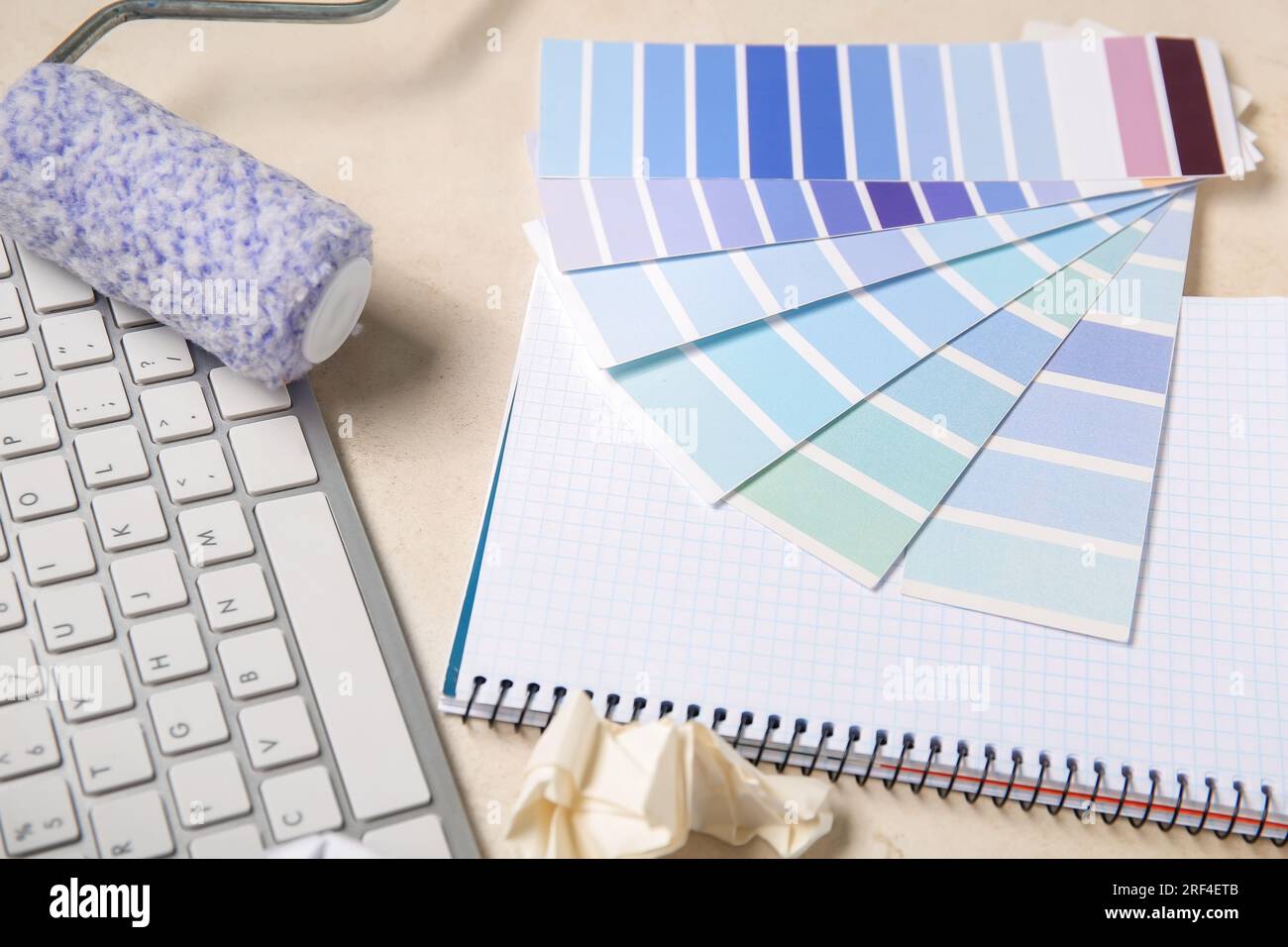 Color palettes, PC keyboard, paint roller and notebook on light ...