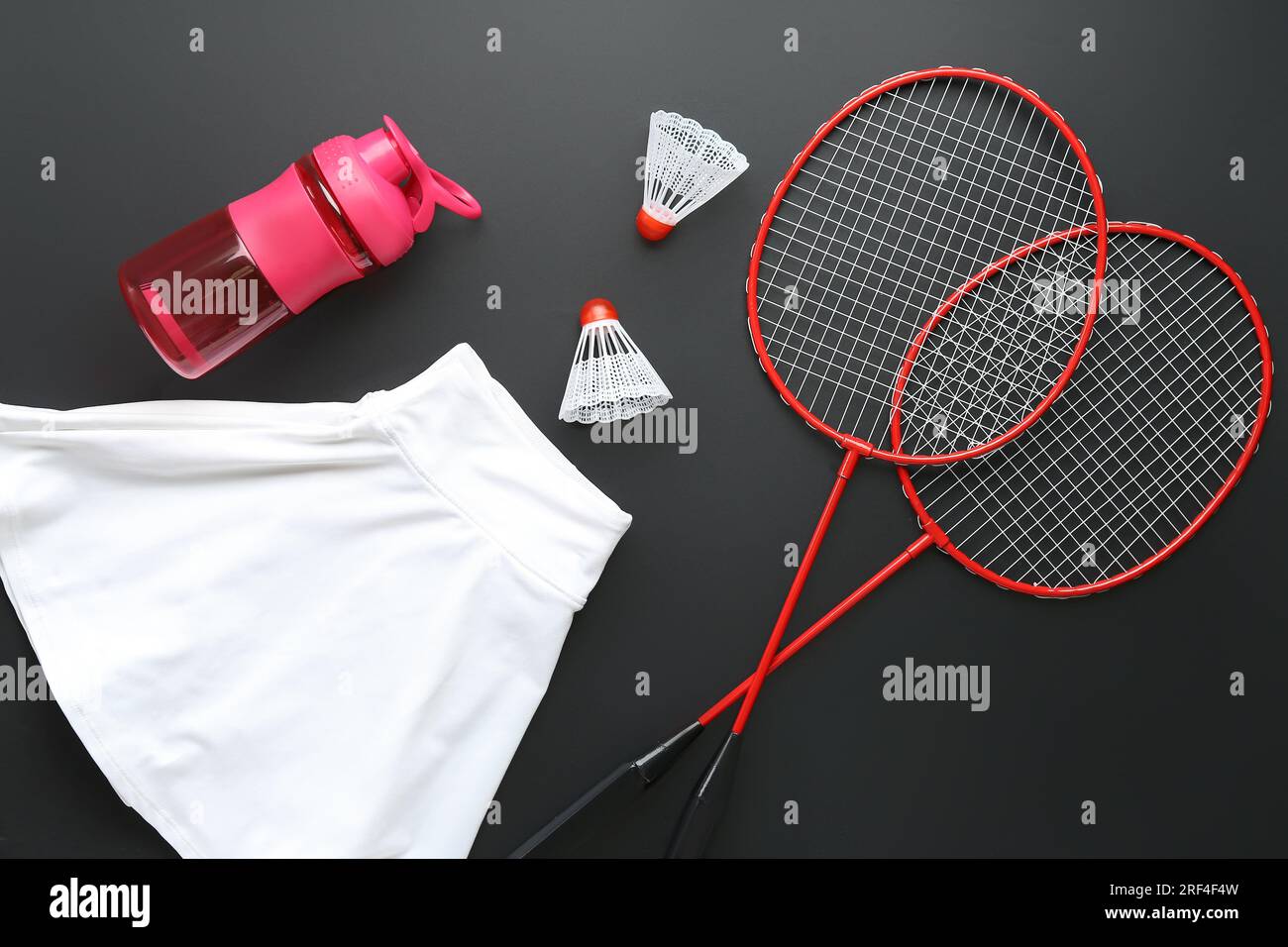 Badminton rackets, shuttlecocks, bottle of water and sportswear on dark ...