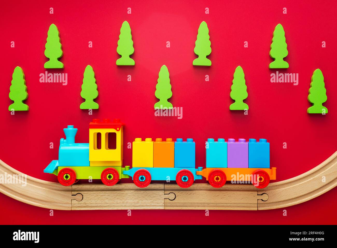 Colorful toy train on wooden railway with green trees on red background ...