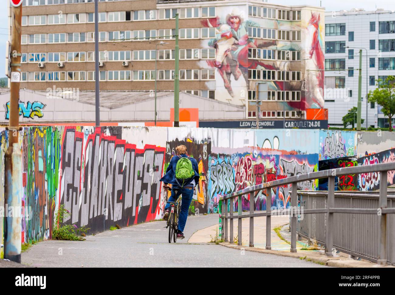 31 July 2023, Hesse, Frankfurt/Main: A man cycles past a wall with ...