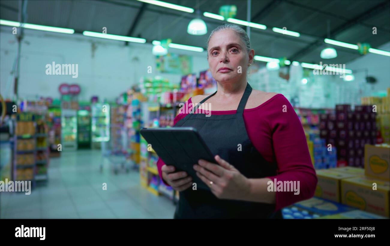 Serious female middle-age employee of supermarket standing inside ...