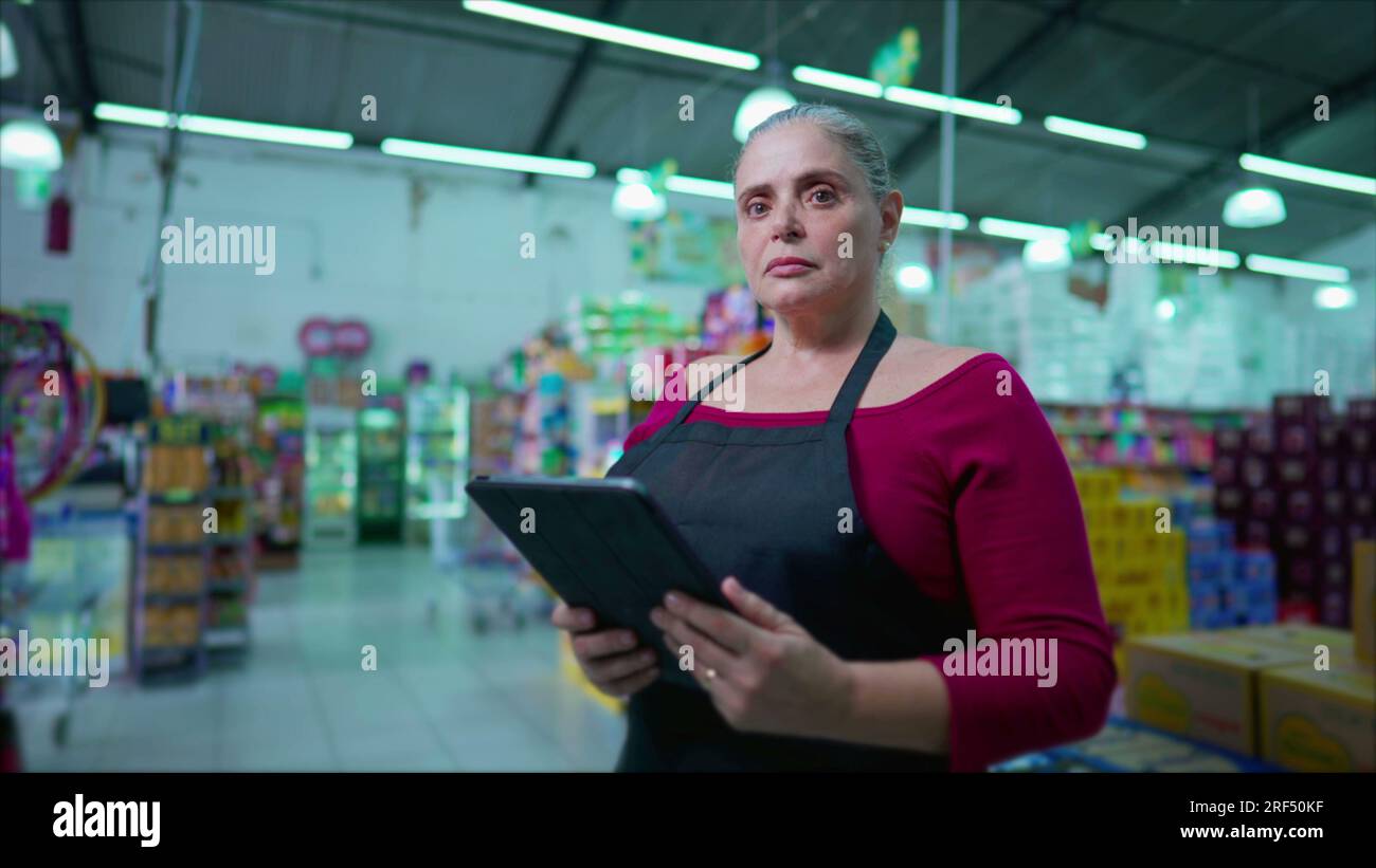 Serious female middle-age employee of supermarket standing inside ...