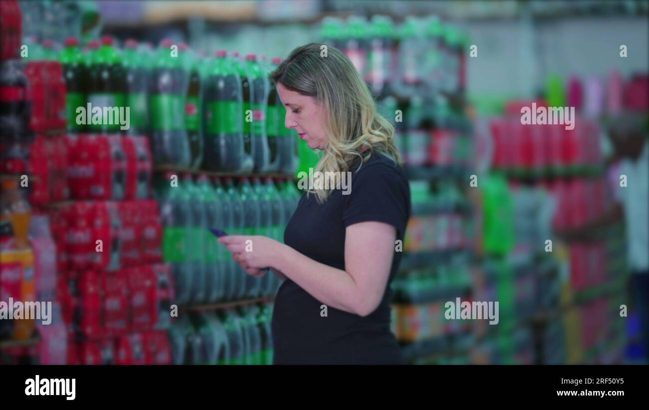 Female consumer walking through supermarket soda drinks aisle holding ...