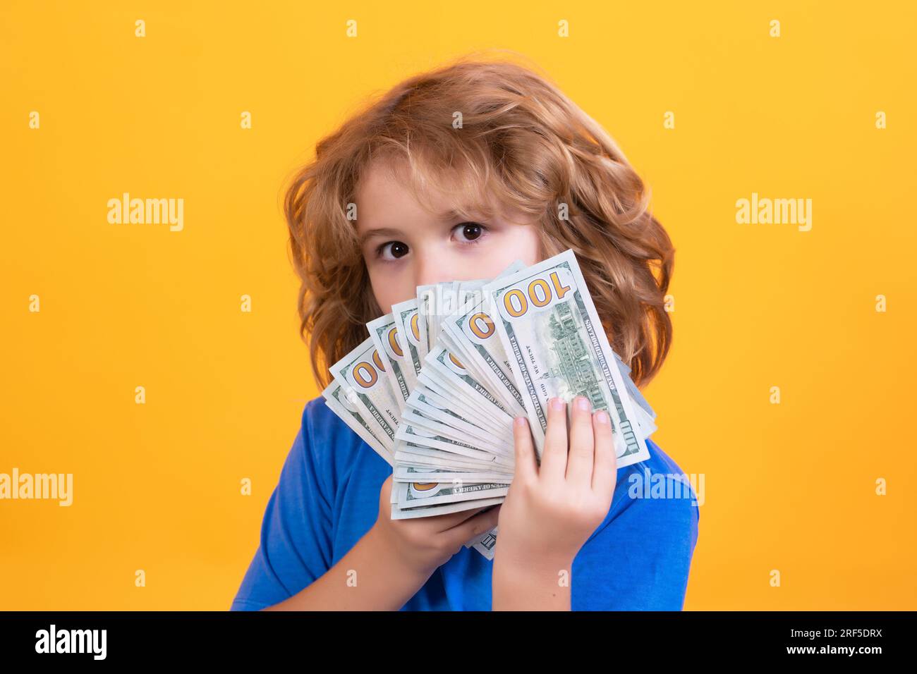 Child with lots of money dollar banknotes isolated over yellow studio ...