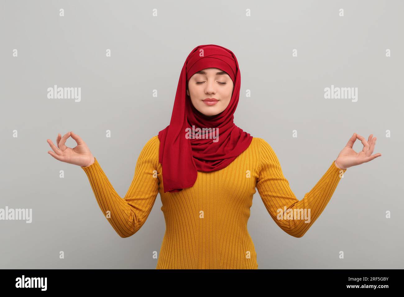 Muslim woman in hijab meditating on light gray background Stock Photo ...