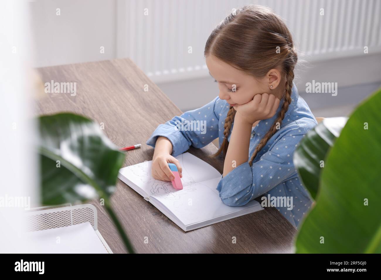 Girl erasing drawing in her book at wooden table in room Stock Photo ...