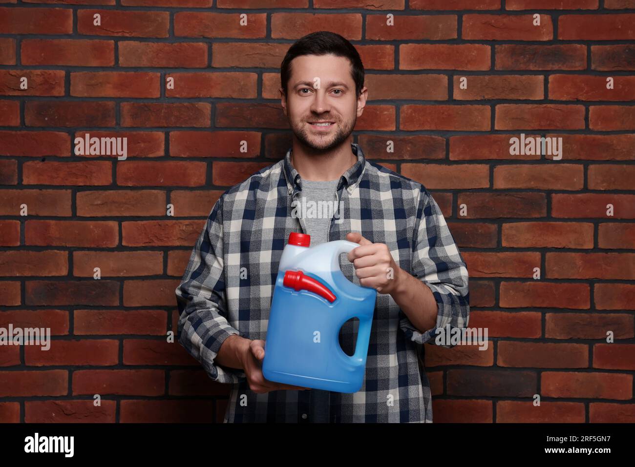 Handsome man holding canister with blue liquid near brick wall Stock ...