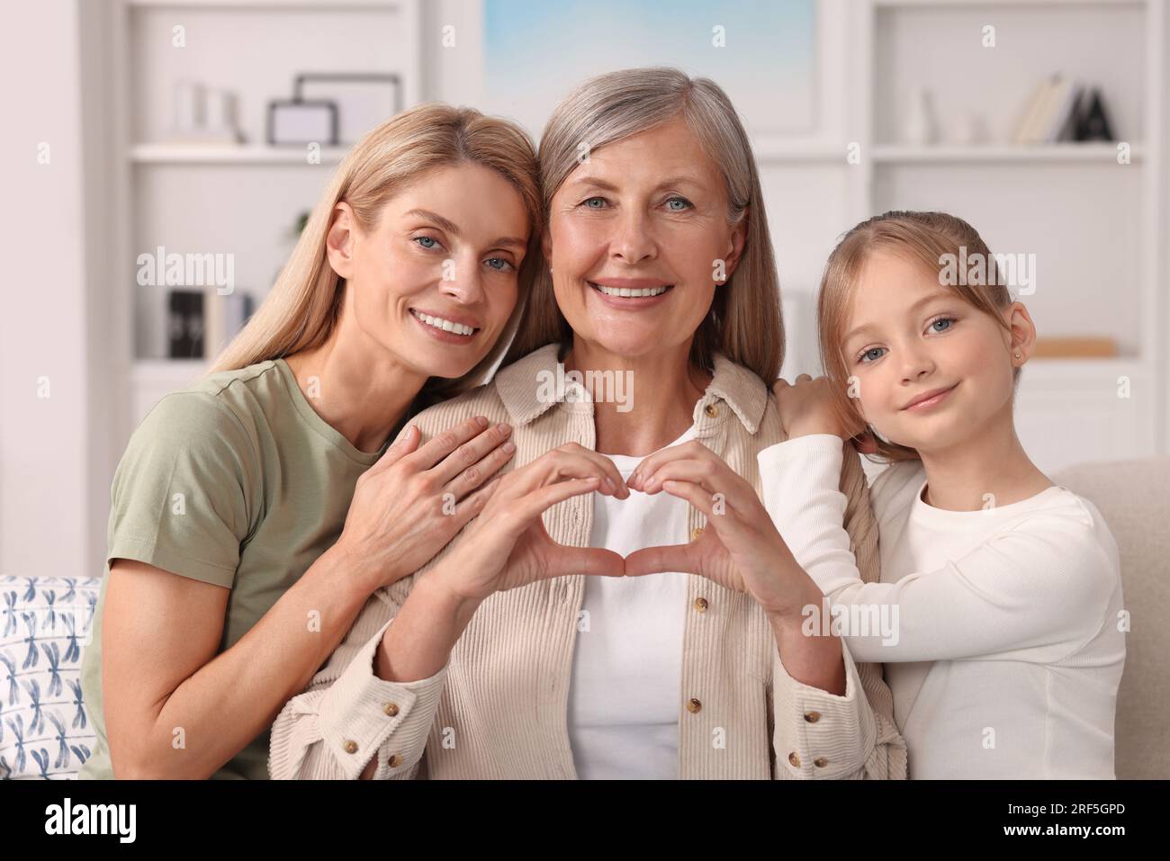 Three generations. Happy grandmother showing heart gesture with her ...