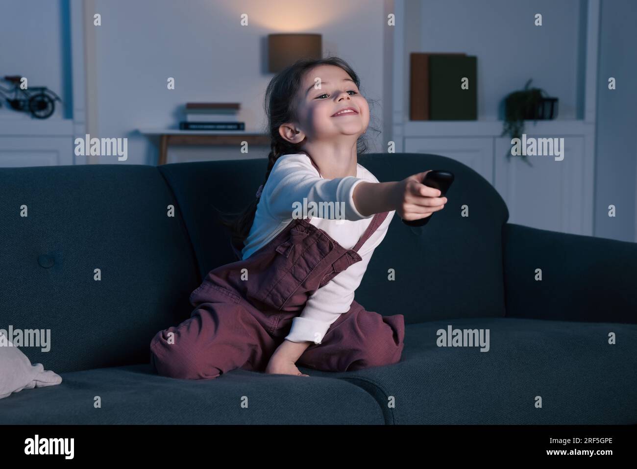 Happy girl changing TV channels with remote control on sofa at home ...