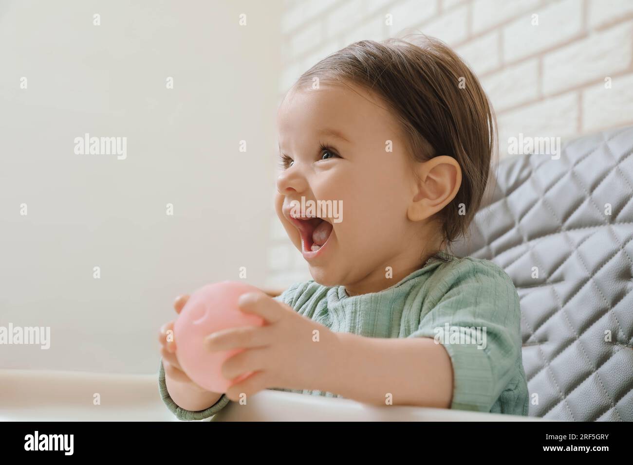 Cute little baby nibbling toy in high chair indoors. Space for text ...