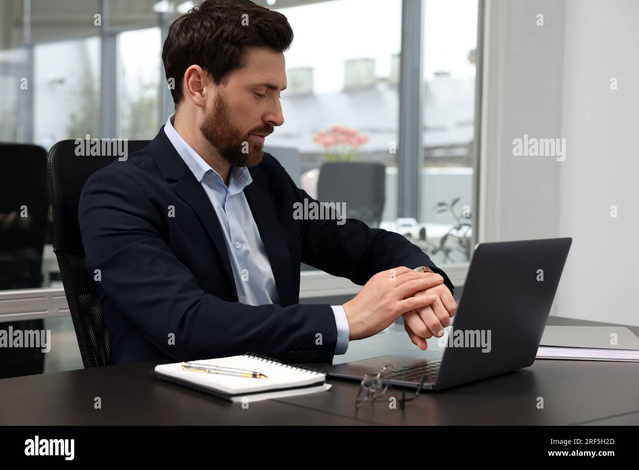 Man checking time on his watch while working with laptop at black desk ...