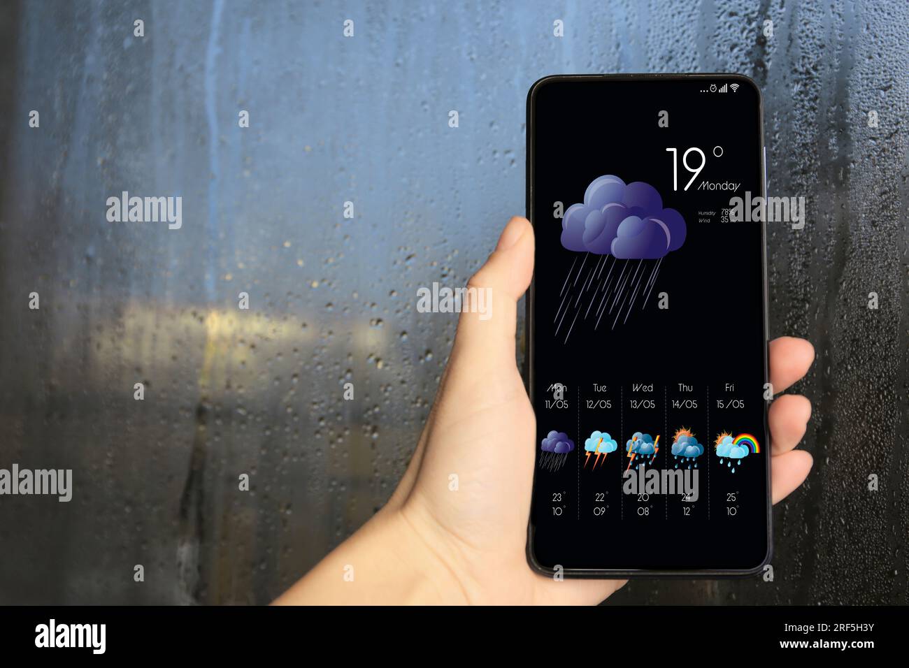 Woman checking weather using app on smartphone near wet window, closeup ...