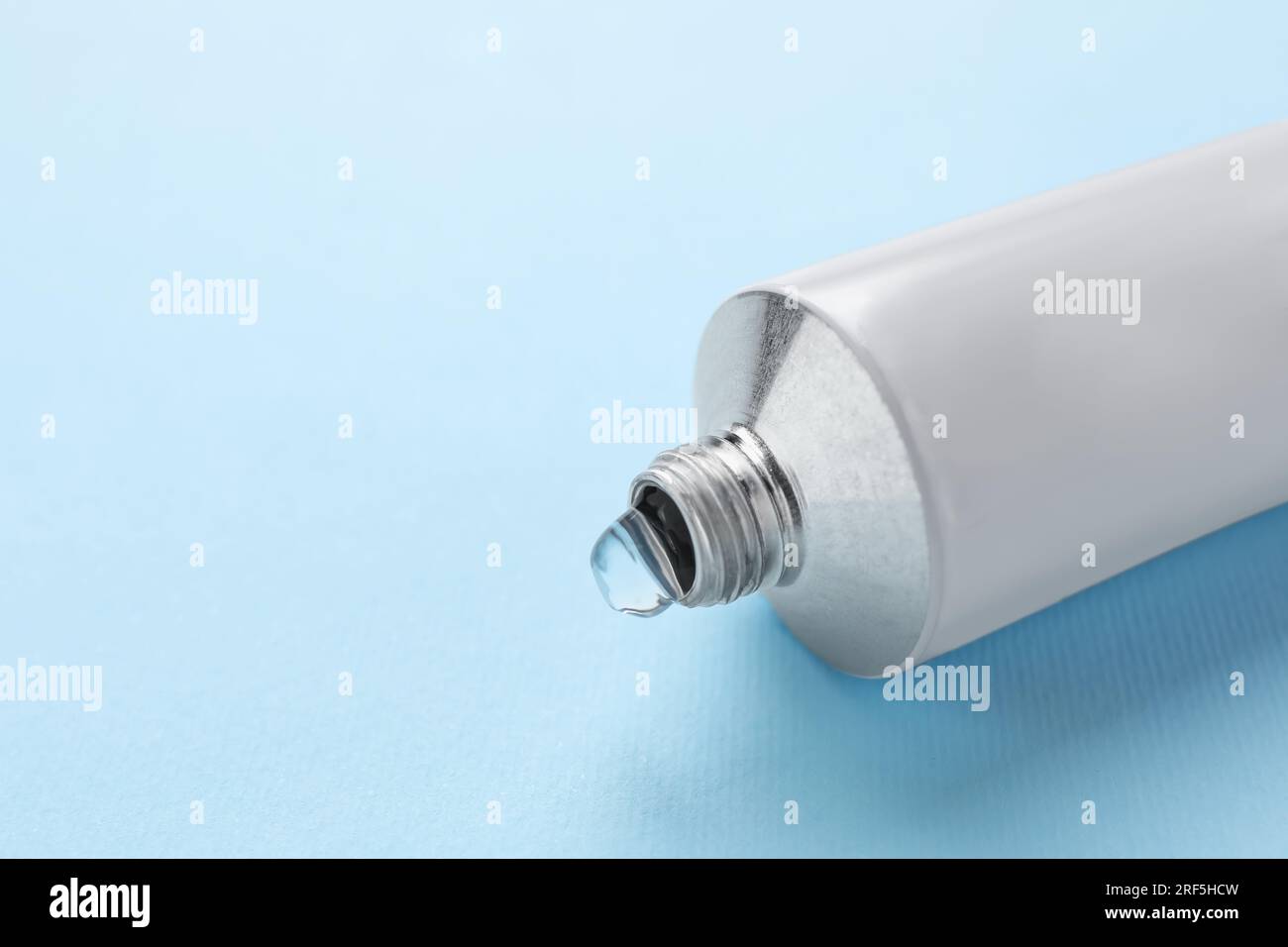 Open tube of ointment on light blue background, closeup. Space for text ...