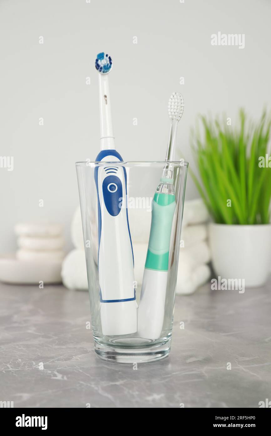 Electric toothbrushes in glass on light grey marble table Stock Photo ...