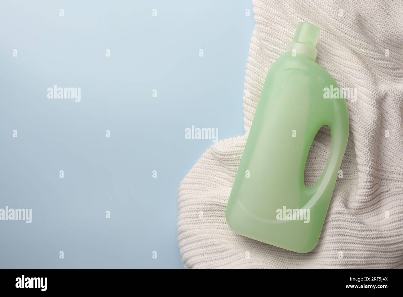 Bottle of fabric softener and white knitted cloth on light background ...