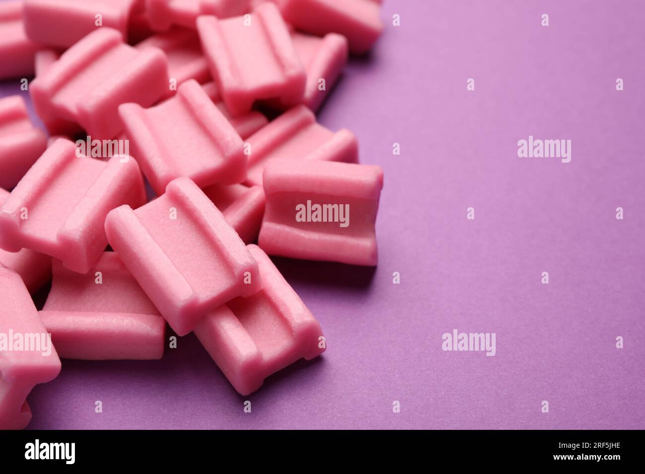 Tasty pink chewing gums on purple background, closeup. Space for text ...