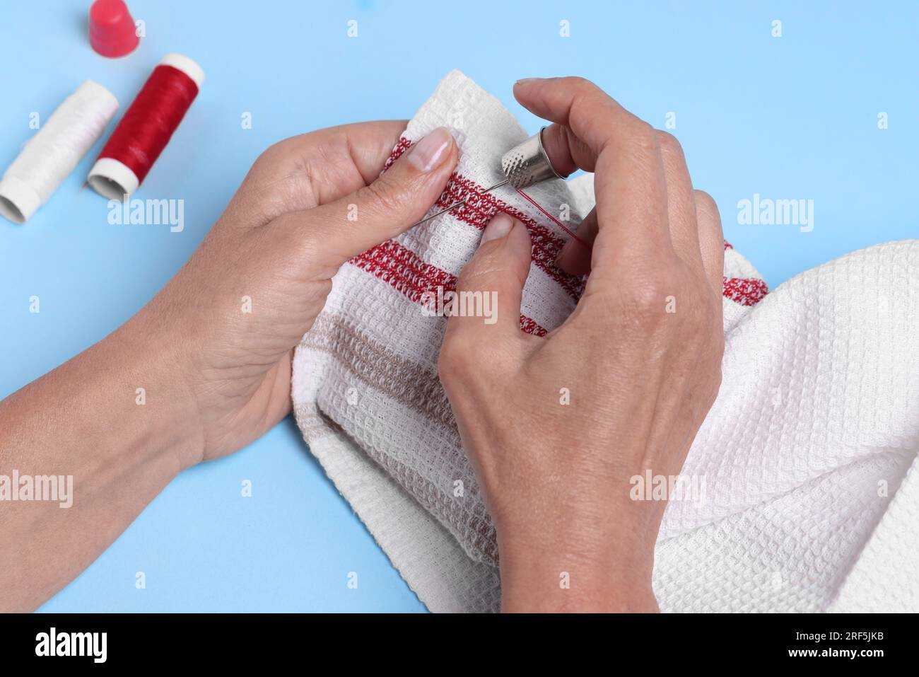 Woman embroidering on fabric with thimble and sewing needle against ...