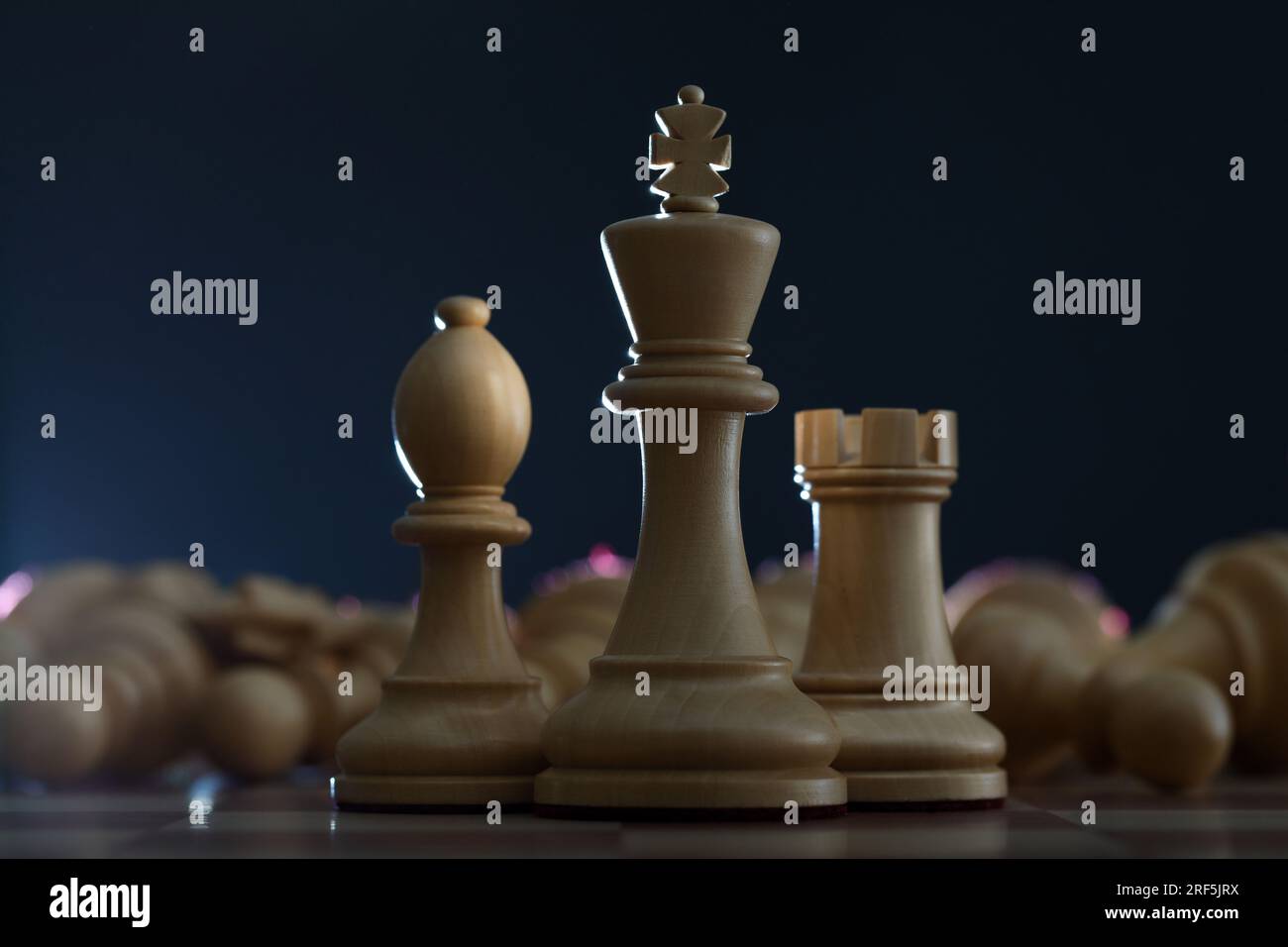 Wooden king, rook and bishop in front of fallen chess pieces on ...