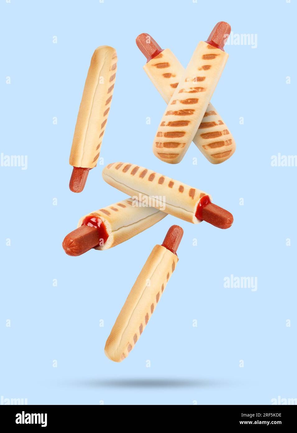 Yummy French hot dogs with grilled buns falling on light blue ...